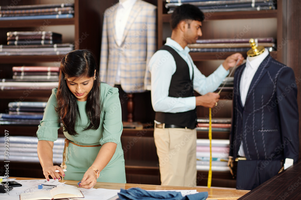 Female tailor checking planner when her colleague measuring bespoke ...