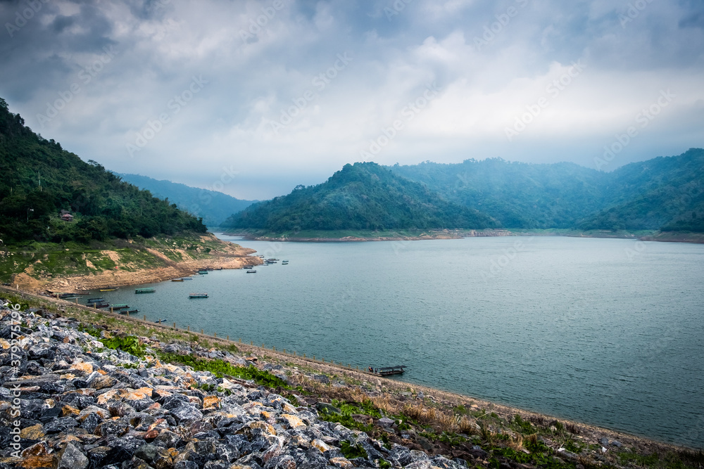 View of Khun Dan Prakan Chon Dam on mountain range next to deep river ...