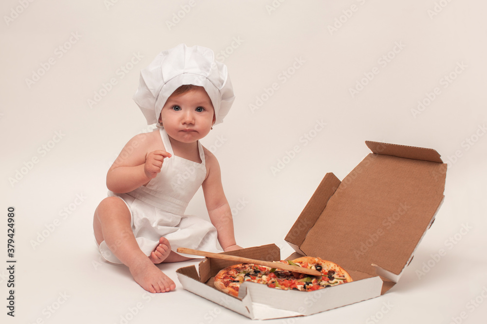 One year old girl dressed as a chef prepares pizza. White background ...