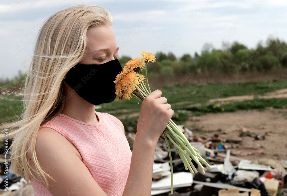 A blonde European girl in a black mask at a dump with flowers in her ...
