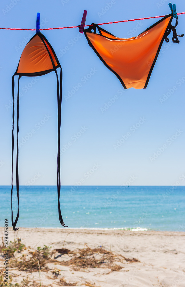 Wet swimsuit on rope with pins on the beach. Orange swimsuit dried on ...
