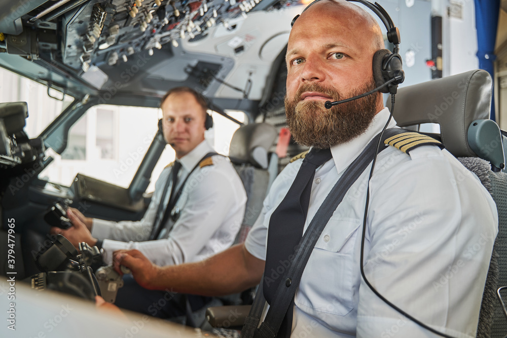 Serious bearded pilot sitting in the cockpit of passenger aircraft ...