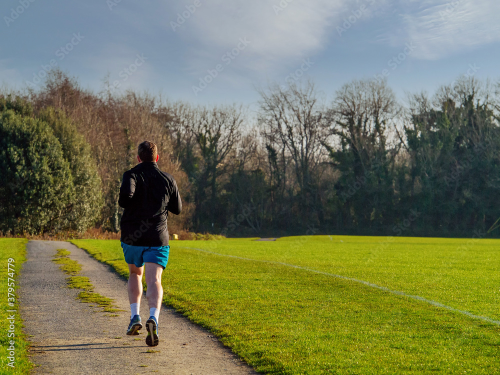 Man jogging in a park by a big green field, Warm sunny day, Blue cloudy ...