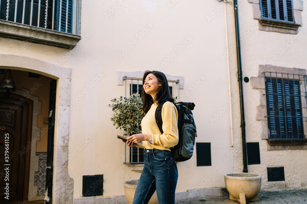 Side view of cheerful female backpacker walking in architecture village ...