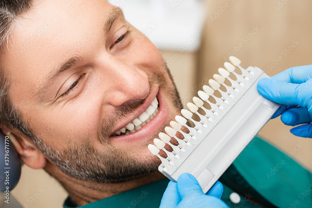 Dentist uses a palette tooth color sample to determine shade of patient ...