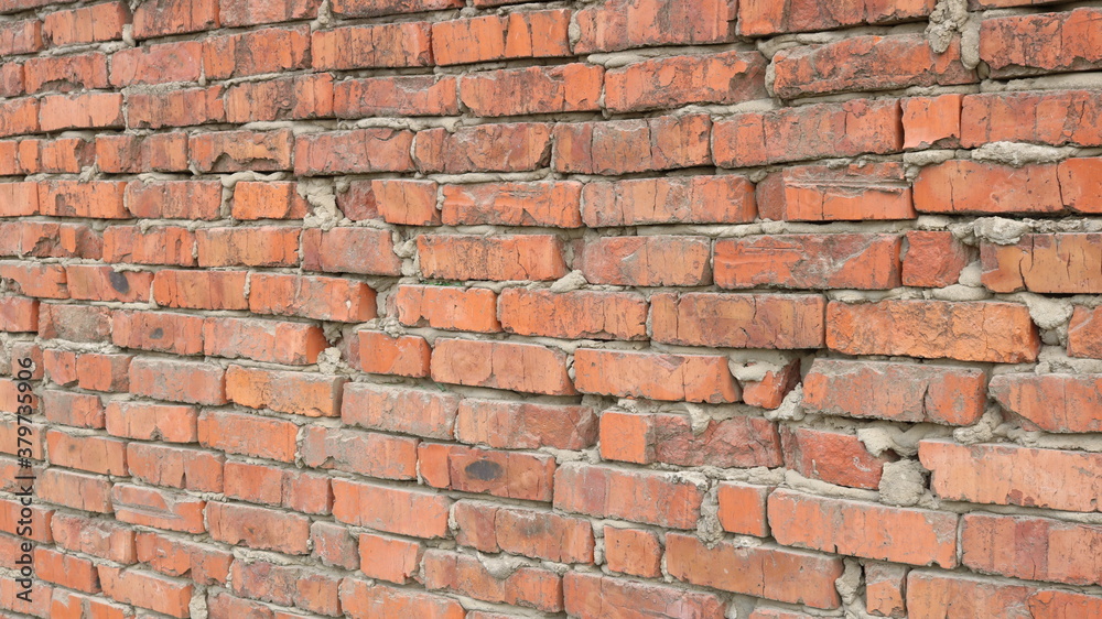 an aging crumbling red brick wall of a building or fence with a rough ...