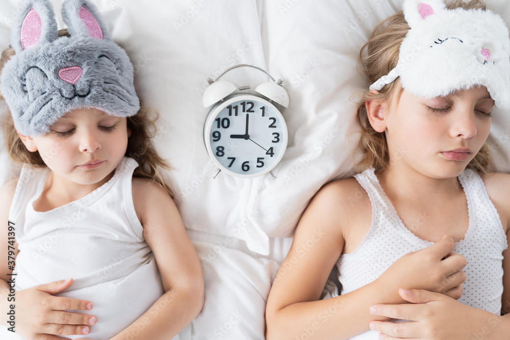 Little girl, sisters sleep in bed with big alarm, clock. Soft cat ...