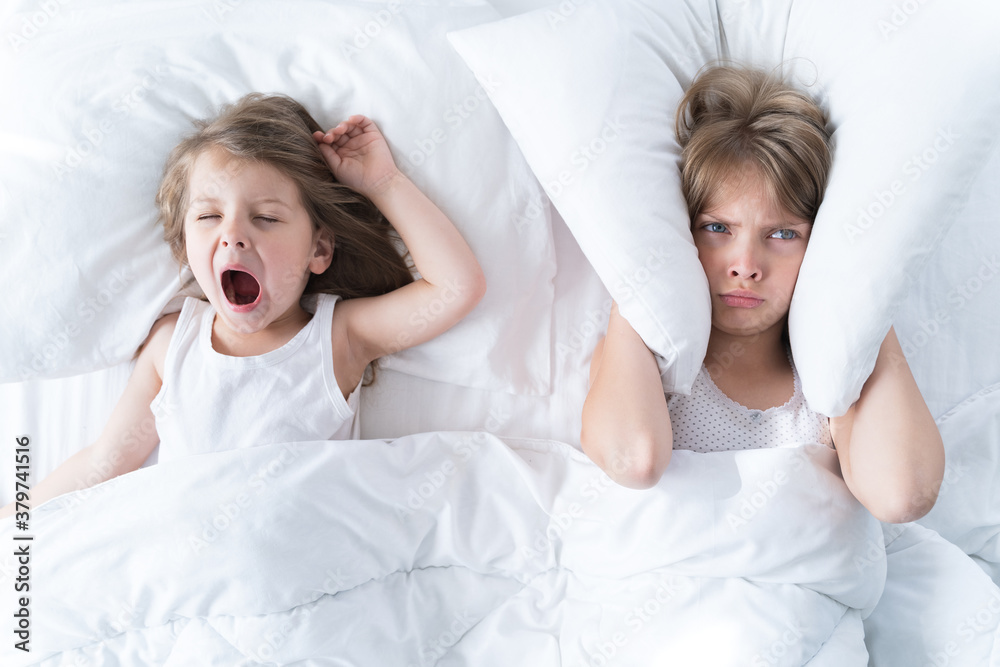 Little girls sleep in bed. One is snoring hard, sister is plugging her ...