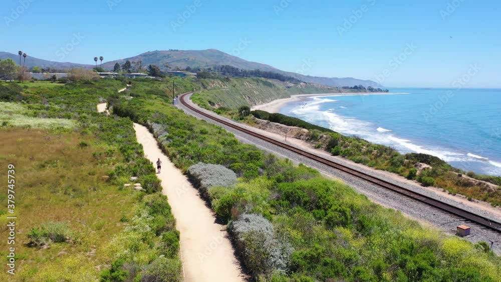 Aerial over man jogging runner exercise along coastal trail, railroad ...