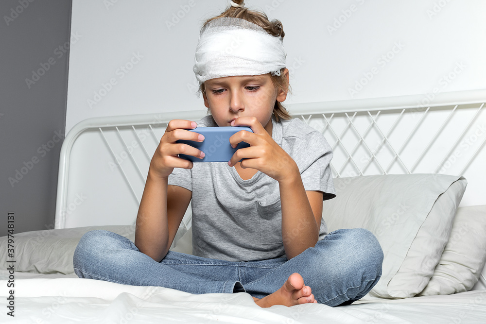 Little Caucasian blond boy with a head injury and bandage is sitting on ...