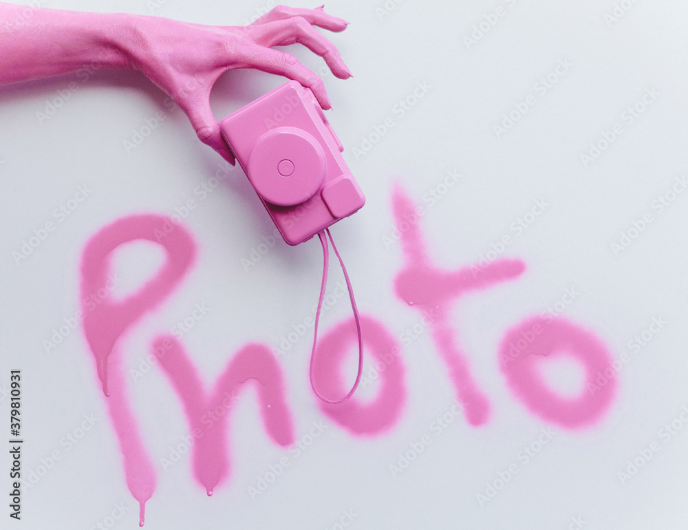 Pink hand holding pink camera over white background with 'Photo ...
