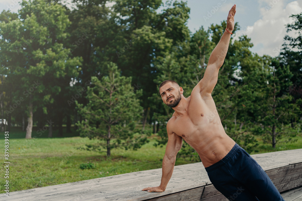 Strong young man stands in side plank on one arm, finds balance, poses ...