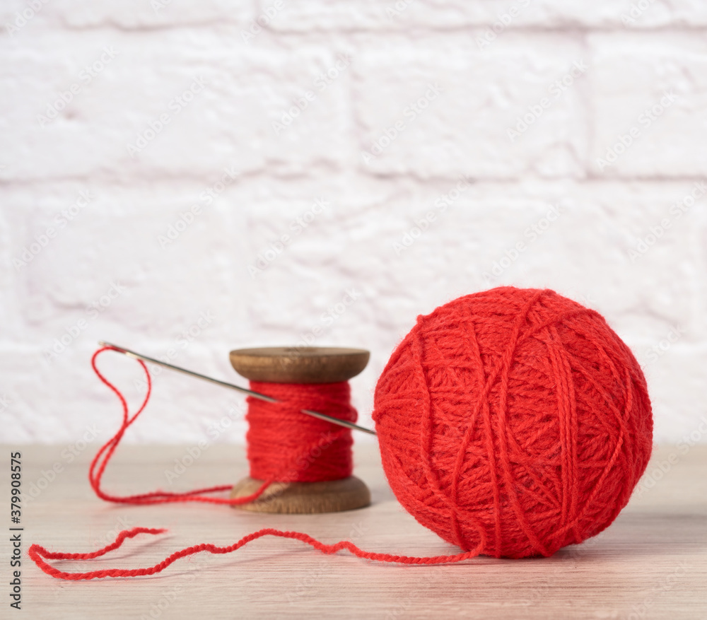 red ball with woolen thread and large needle on white brick wall ...