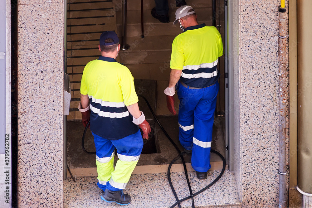 sewer utility workers with hose and pressurized water working inside a ...