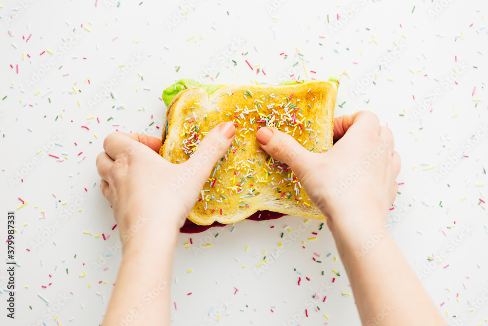 Hands pick up grilled cheese sandwich, rainbow coloured with spr Stock ...