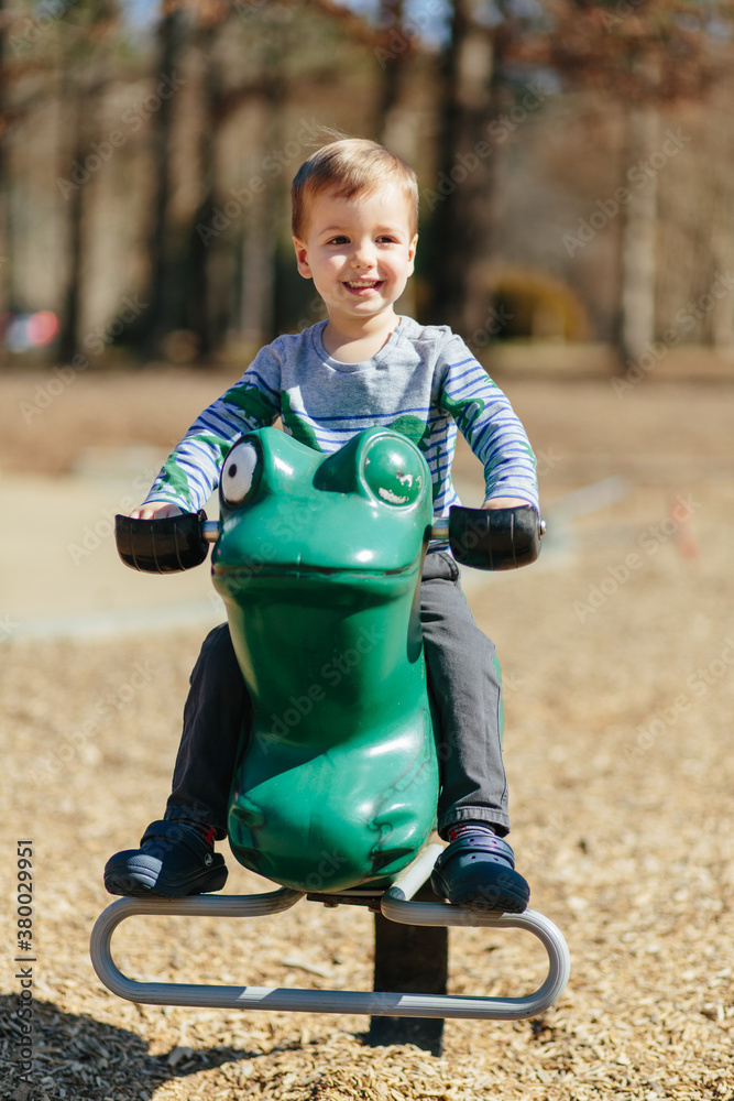Cute young boy riding a one eyed frog toy in a park Stock Photo | Adobe ...