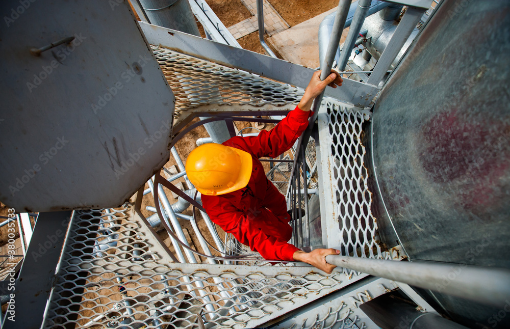 Oil refinery worker in red work wear and yellow helmet on grey grid ...