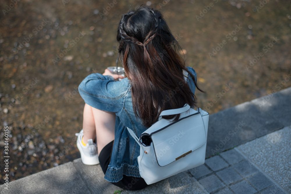 A young girl sitting with her back facing the camera in a jean jacket ...