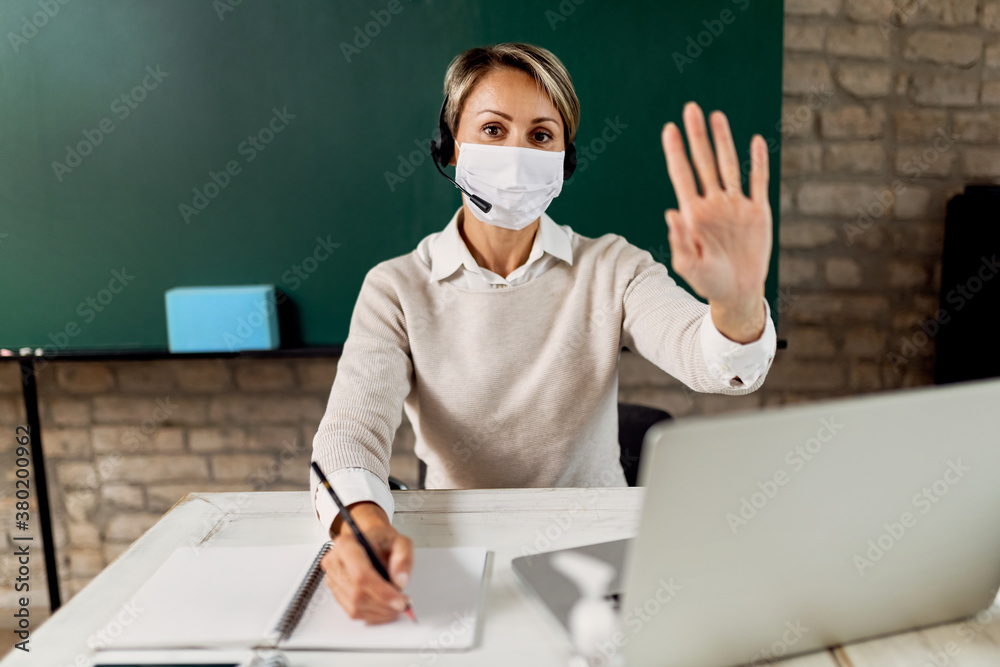 Female teacher with face mask taking notes and waving from the ...