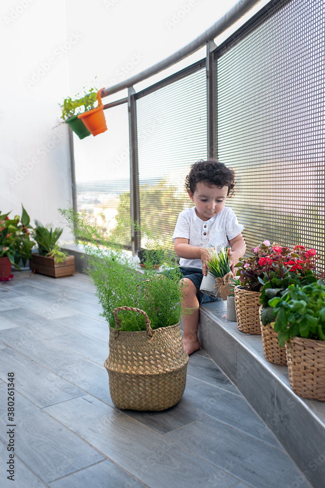 Little child taking care of plants on the balcony. Toddler in terrace ...