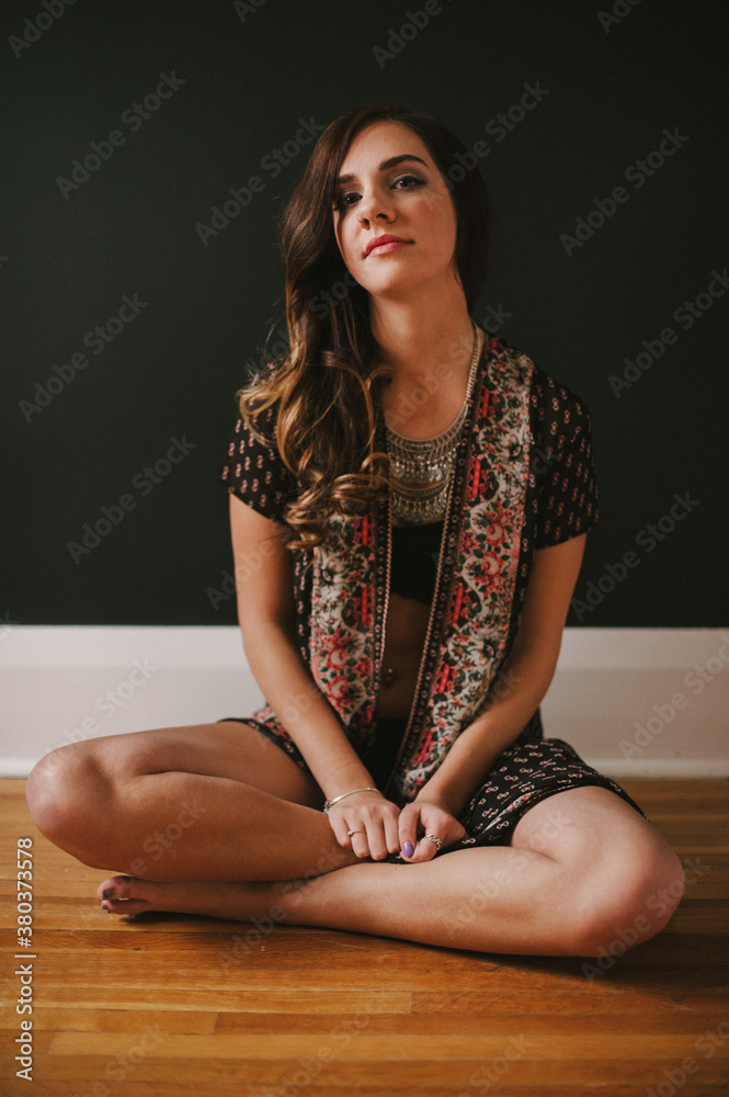 Young attractive bohemian model sitting cross legged on old wood floor ...