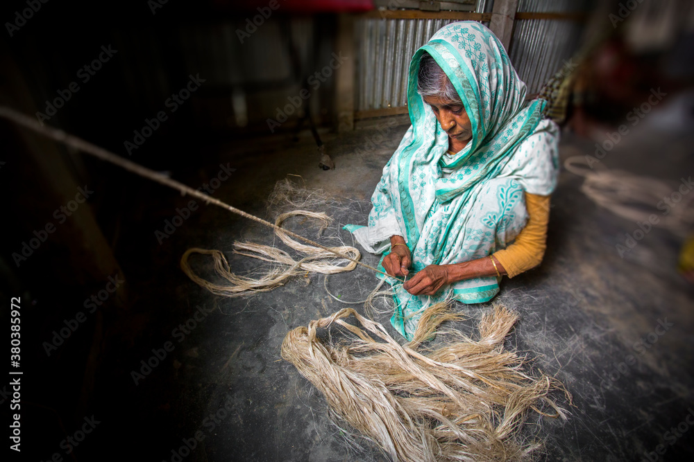An old age woman is making a rope from the banana tree fibers in her ...