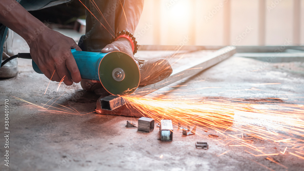 Selective focus at worker hand using angle grinder cutting square tube ...