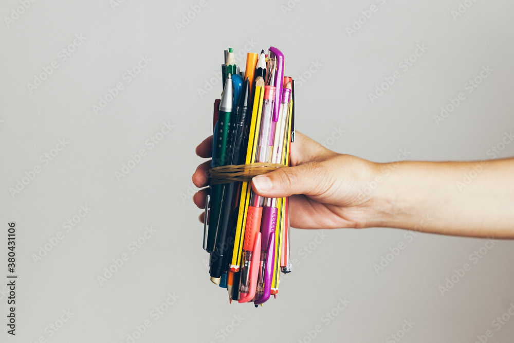 Back to school. Hand holding stack of pens and pencils with a rubber ...
