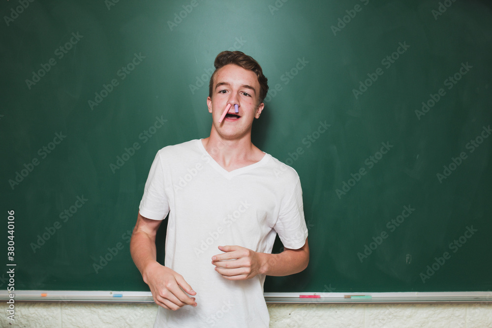 High school student standing in front of green chalkboard with chalk up ...