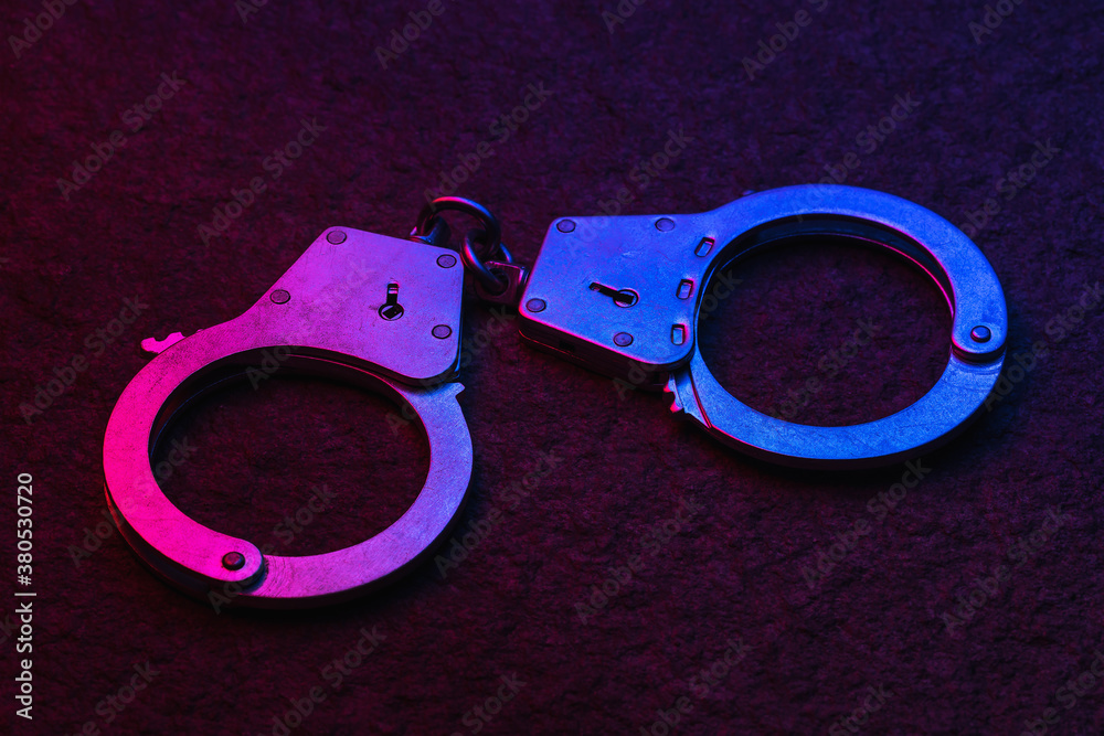 Handcuffs on a stone surface illuminated by flashing lights of a police ...