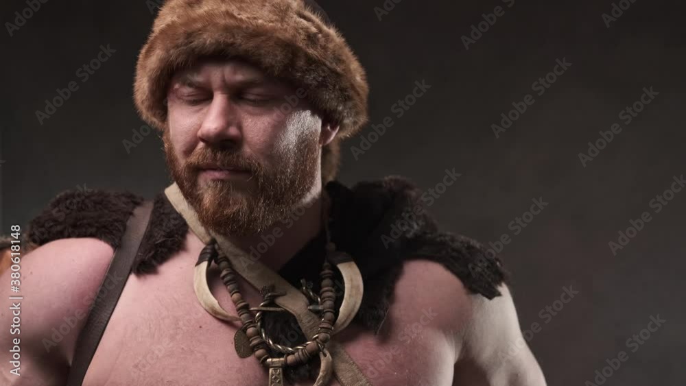 Serious Viking clad in light armor with a shield behind his back holds ...