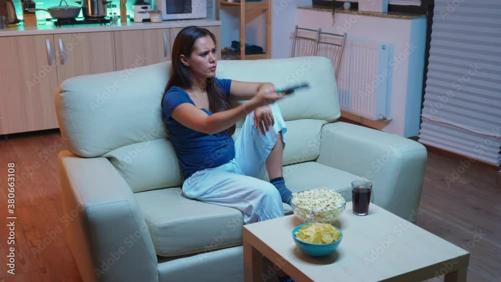Nervous woman with television remote control sitting on the sofa. Bored ...