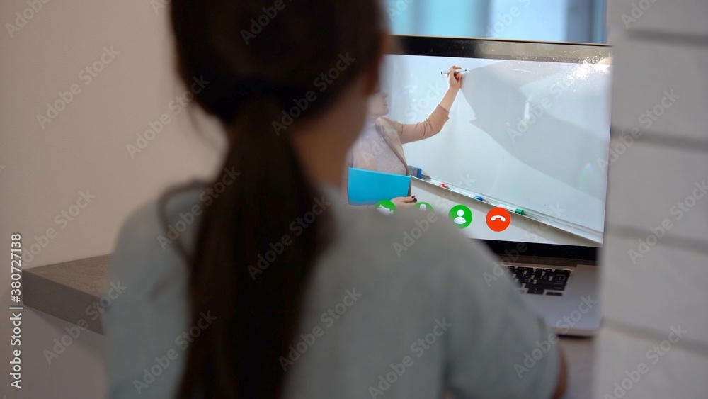 Little girl of school age is studying at home. A girl watches a video ...