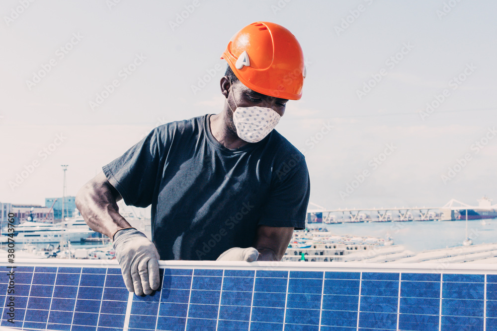 Black workman in helmet and protective mask installing solar battery in ...