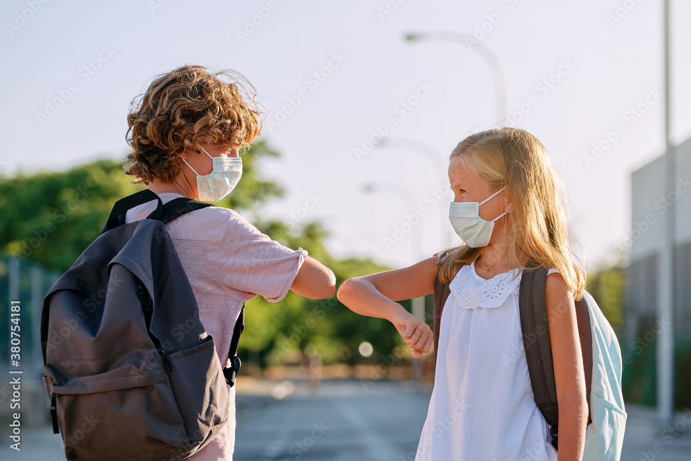 Two kids with school bags and masks greeting each other with a gesture ...