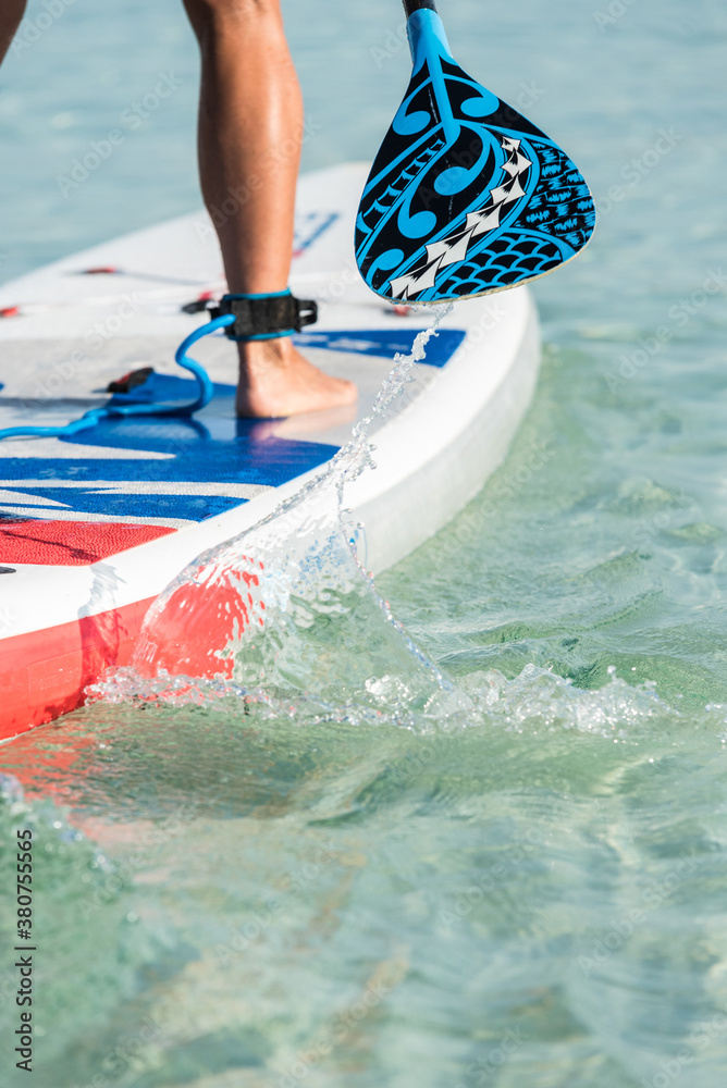 Crop anonymous female surfer standing on surfboard and rowing with ...