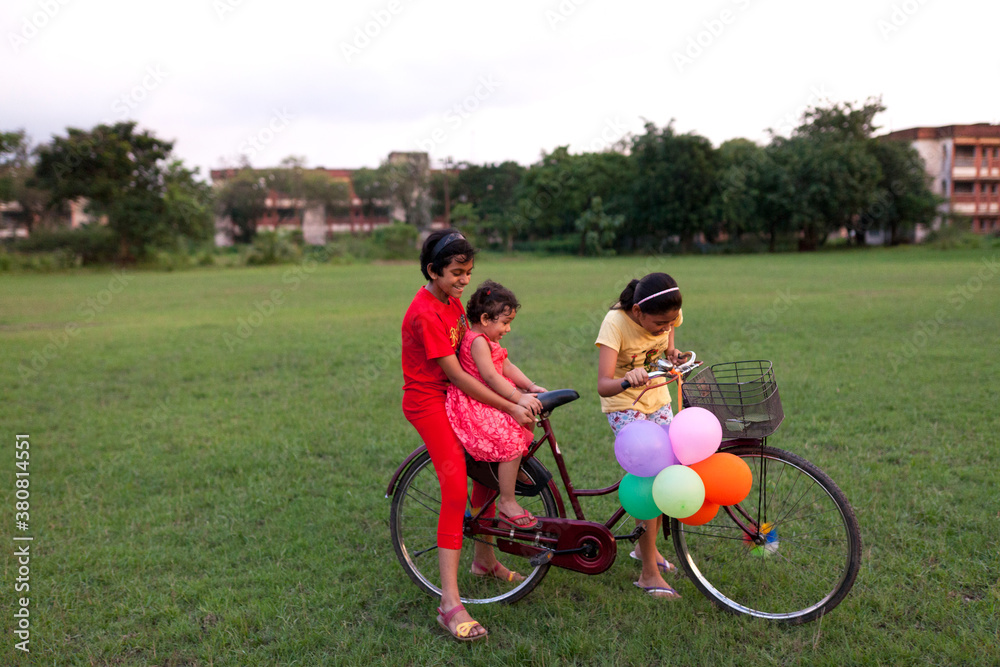 Teenage girls and a kid playing with cycle in a green field Stock Photo ...
