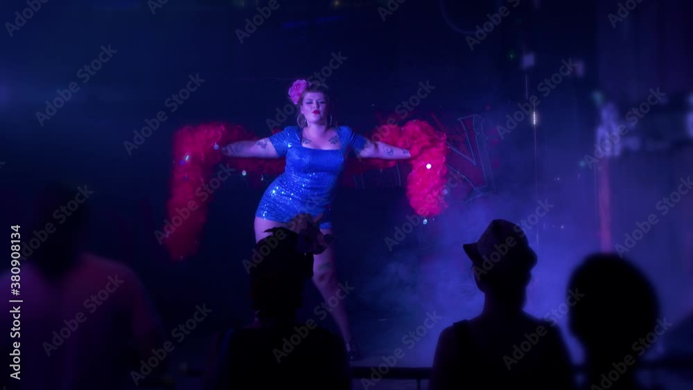 Curvy burlesque dancer makes an entrance on stage with a red feather ...