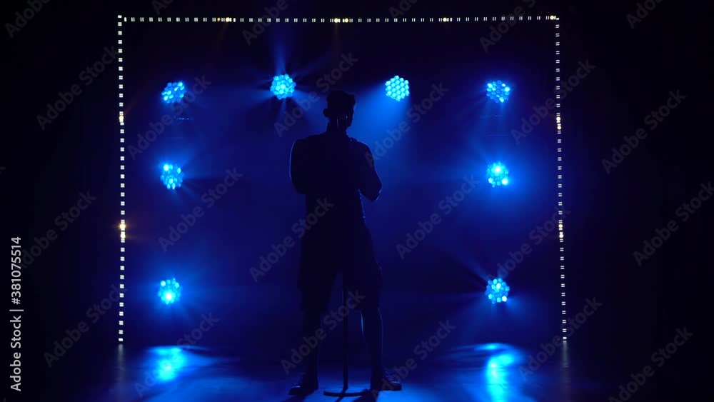 Young guy rock star sings into a microphone in a dark studio at night ...