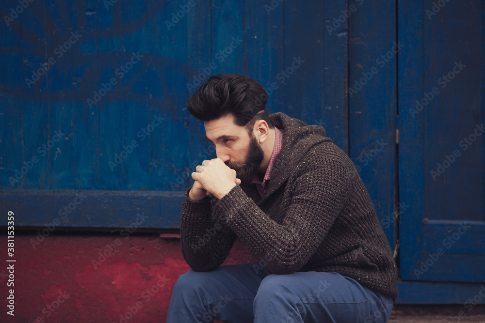 Stressed and upset young man sitting outside holding head with a hand ...