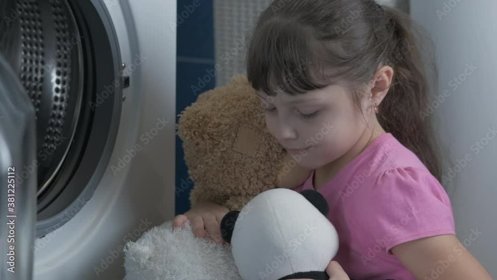 Child wash in a machine. A happy child puts her toys into a washing ...