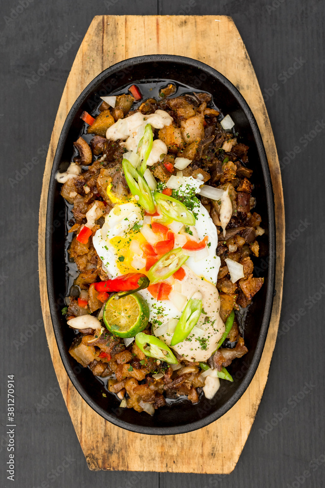 Top view of Freshly cooked Pork Sisig with egg, onions and chilies. A ...