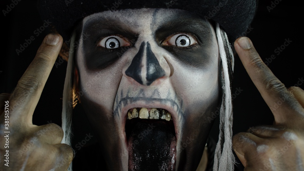 Sinister man with skull makeup making faces and showing middle finger ...