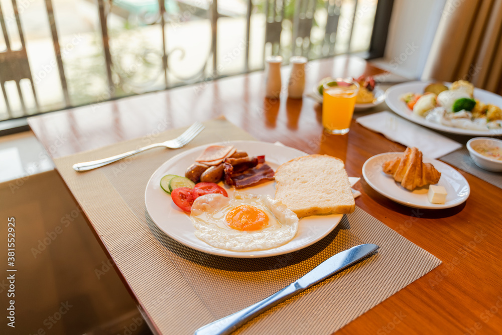 Fresh breakfast table next to window with bread, pastry, egg, fruit ...