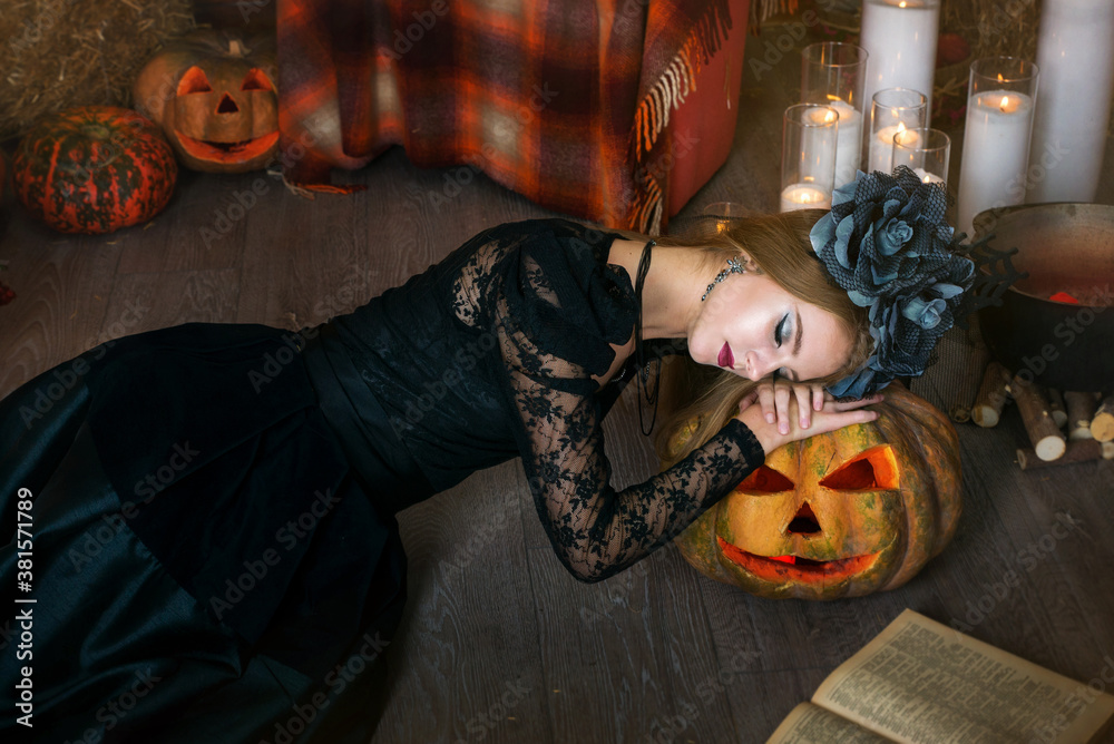Halloween Witch girl sleeping with her head on a pumpkin lying next to ...