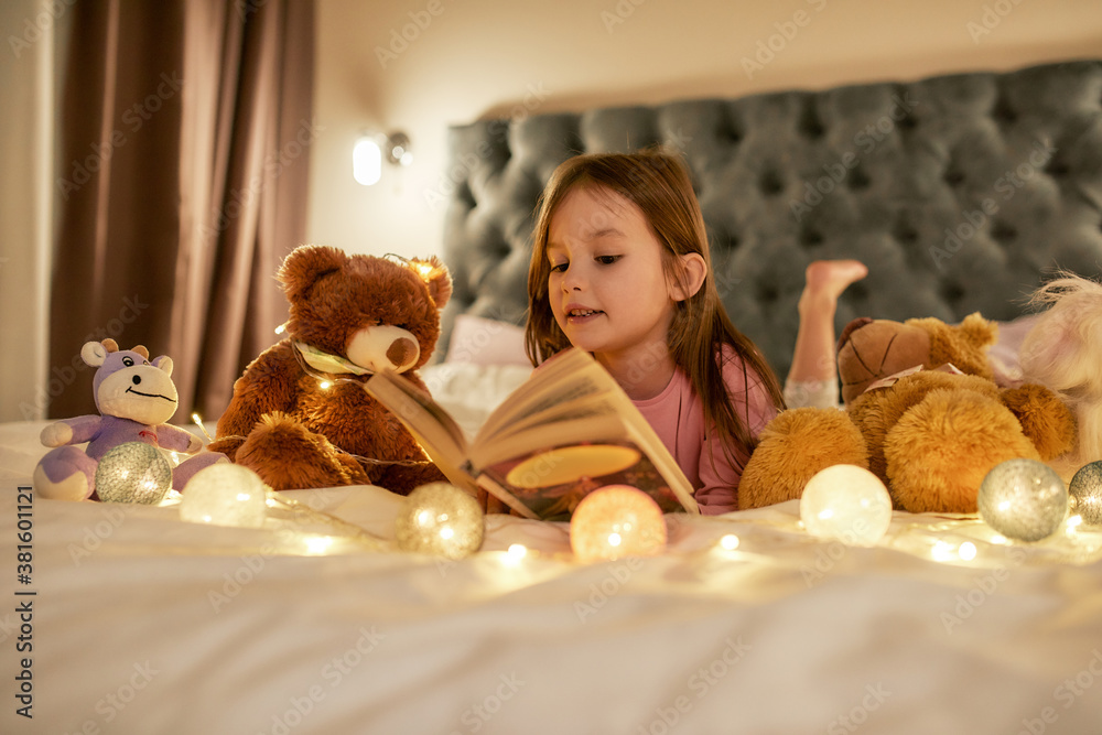 A cute girl is lying on her stomack in a huge bed barefoot reading a ...