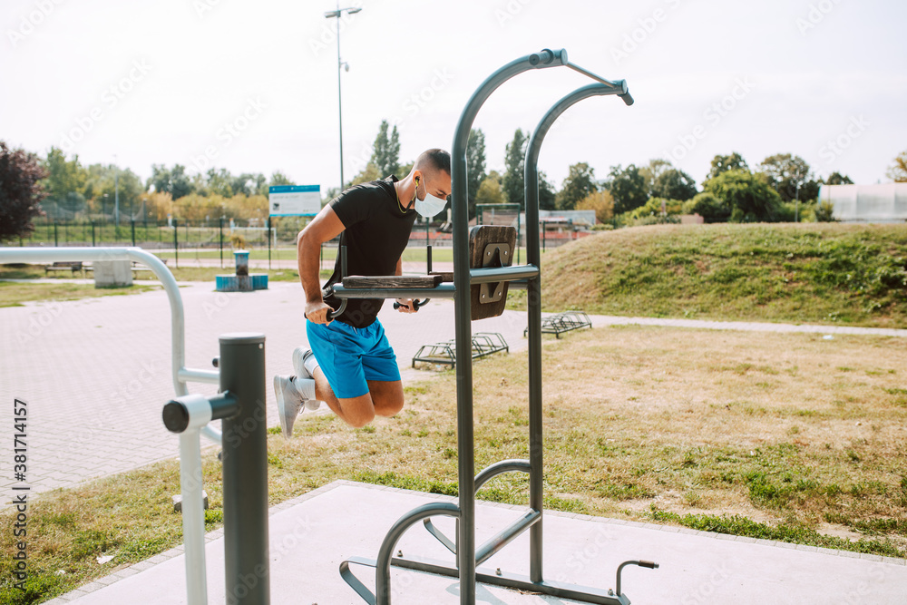 Fit young male caucasian athlete with face mask trains on arm and leg ...