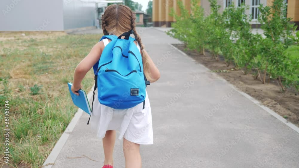 little girl kid with a backpack and a textbook runs hurrying to school ...