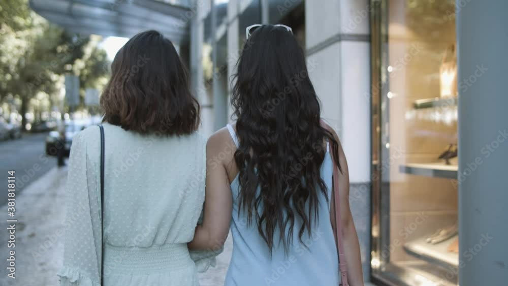 Back view of two young women walking together. Brunette ladies going ...