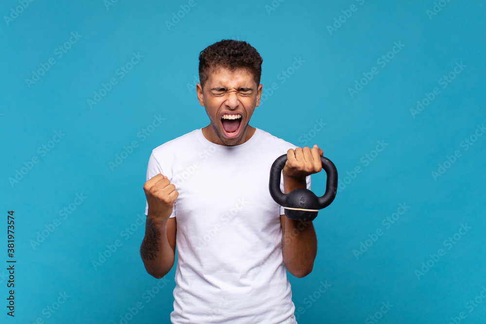 young man lifting a sumbbell shouting aggressively, looking very angry ...